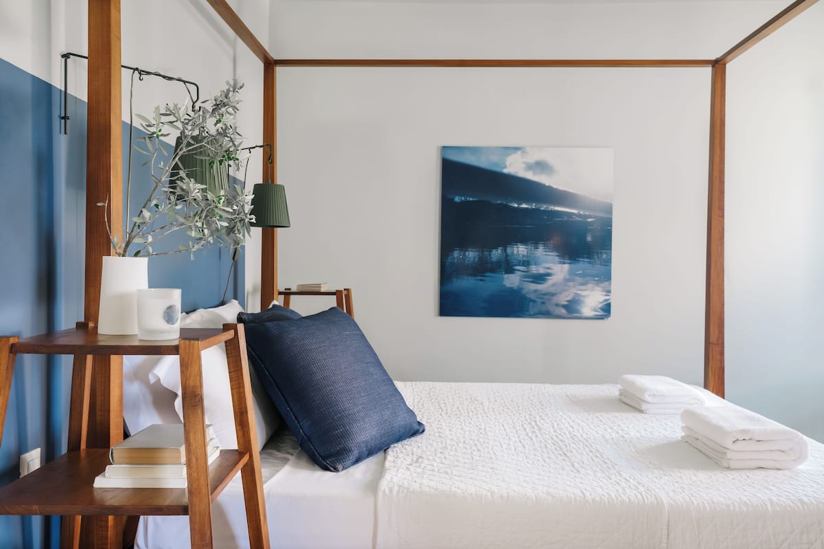 Quarto bem arrumado com cama, travesseiros, mesa de cabeceira com uma planta, abajur e um quadro na parede.