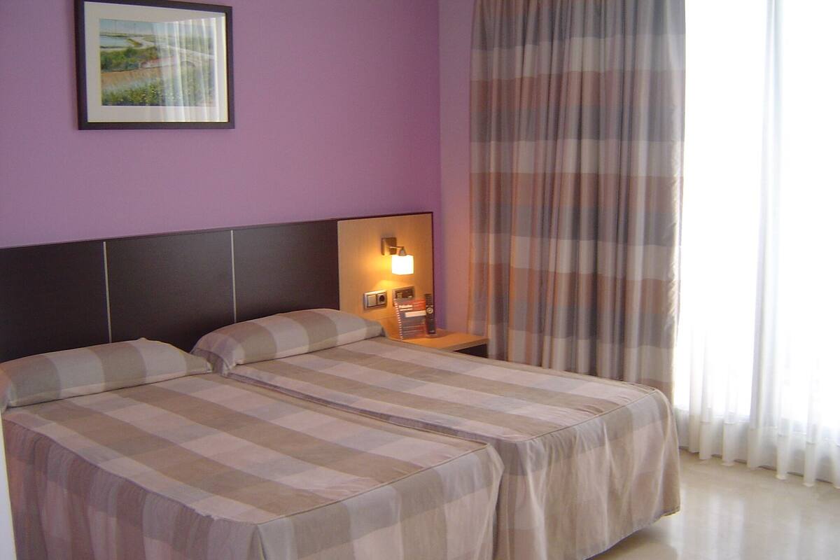 Uma cama de casal com cabeceira, uma mesa de cabeceira com abajur e um quadro na parede.