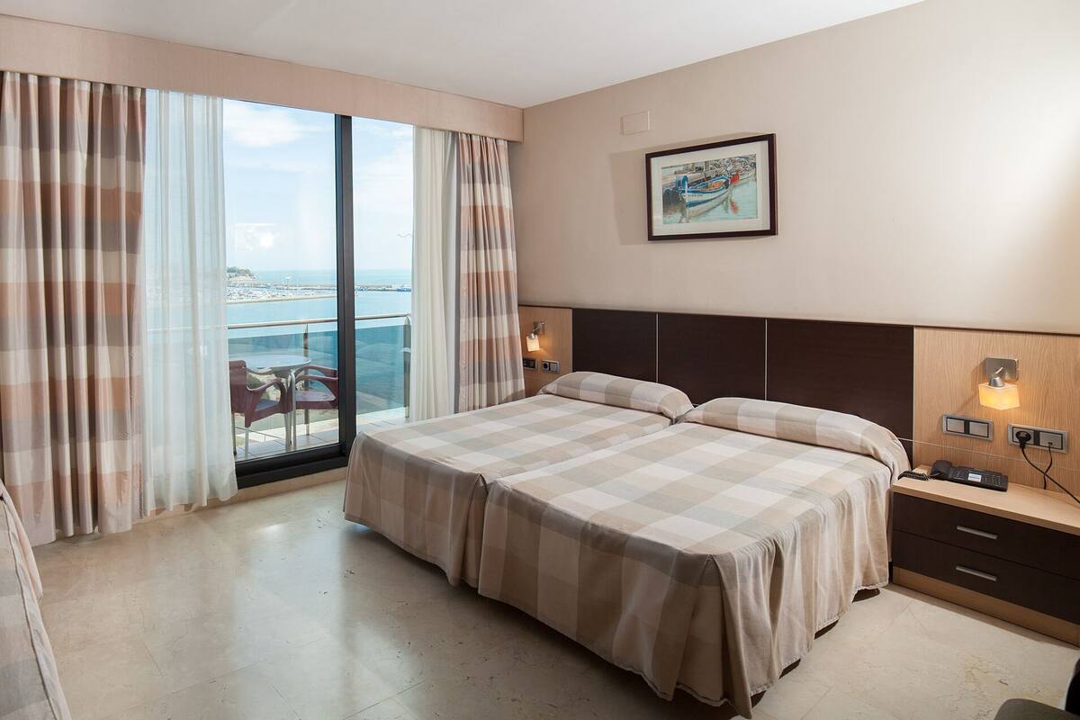 Quarto de hotel com duas camas, varanda e vista, e um quadro na parede.
