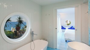 Uma casa de banho com banheira, espelho redondo e vista para uma varanda com cama.