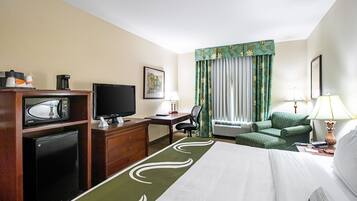 Quarto de hotel com cama, escrivaninha, cadeira, televisão, frigorífico e janela com cortinas.