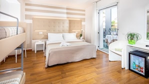 Quarto de hotel moderno com uma cama grande, uma escrivaninha com computador, um mini frigorífico e uma porta de vidro deslizante para a varanda.