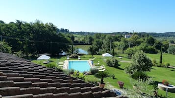 Piscina com vista para um lago, rodeada por vegetação e céu claro.