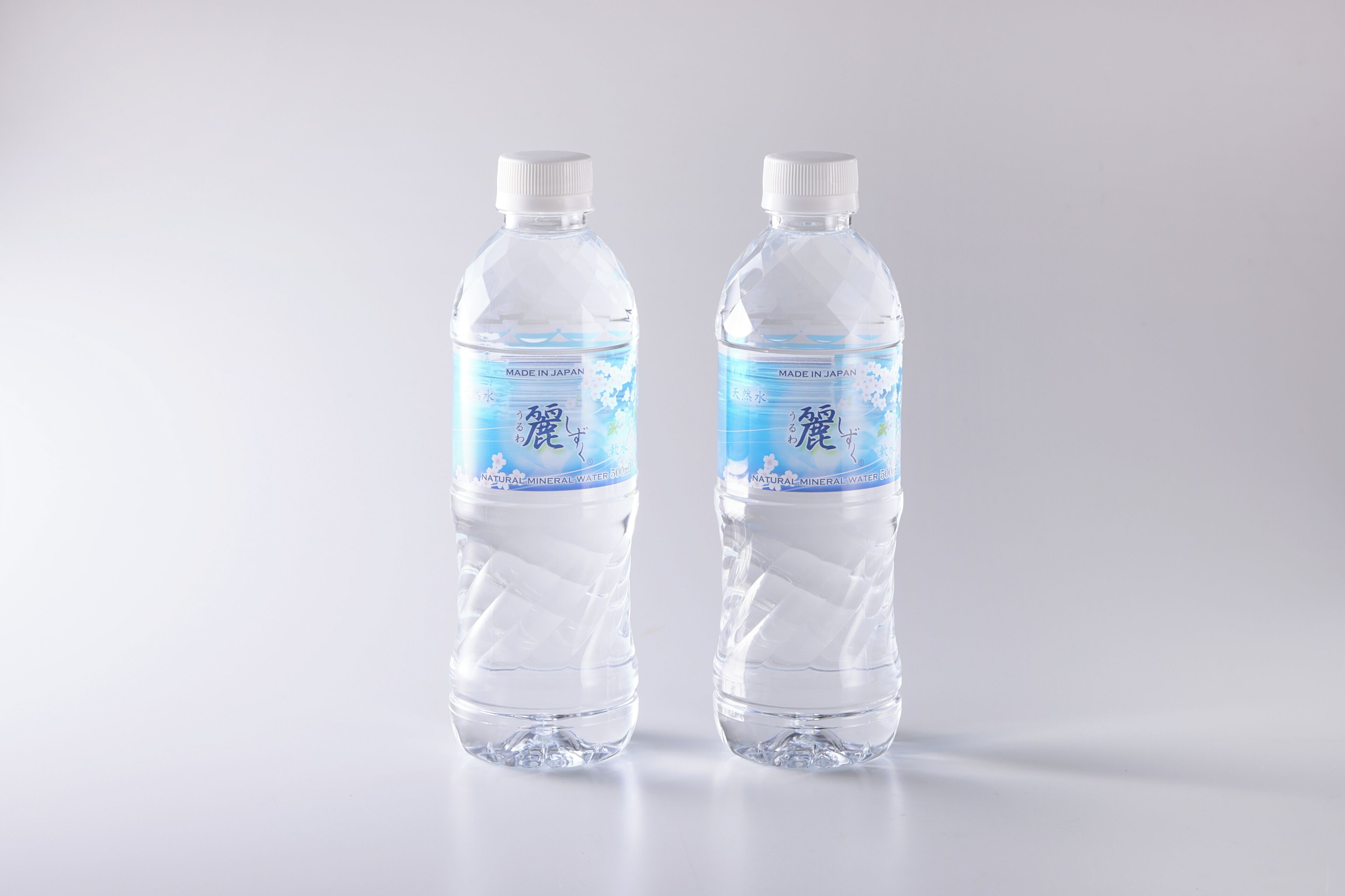 Duas garrafas de água plásticas transparentes, com etiquetas, em pé sobre uma superfície plana.