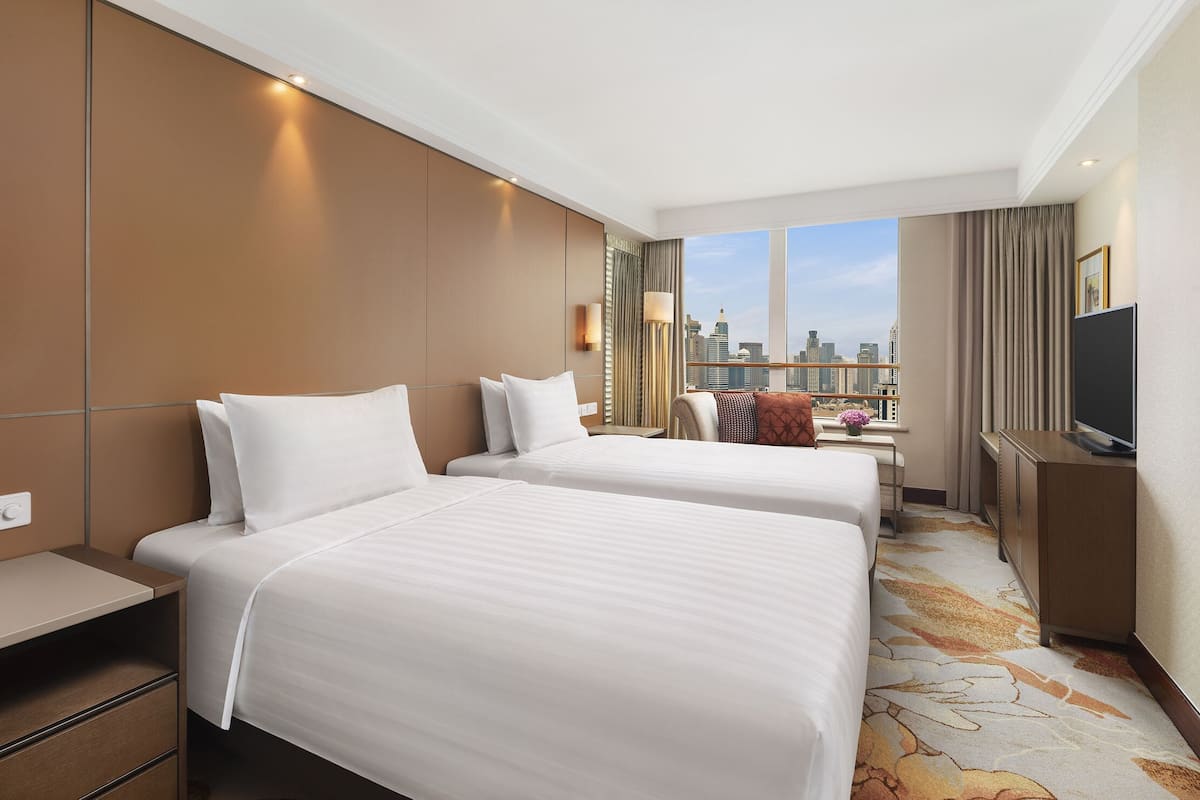 Quarto de hotel com duas camas, uma escrivaninha, uma cadeira, uma televisão e vista para o horizonte da cidade.
