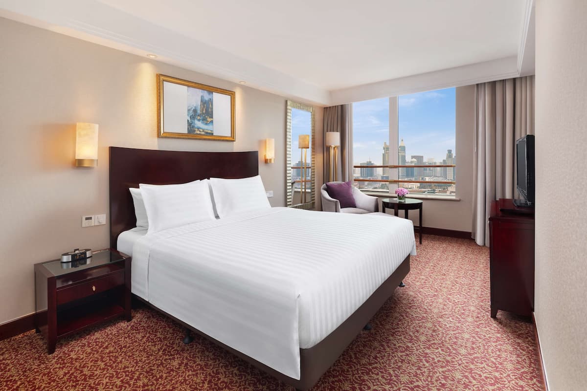 Quarto de hotel com uma cama grande, uma escrivaninha, uma cadeira, uma televisão e vista para a cidade.