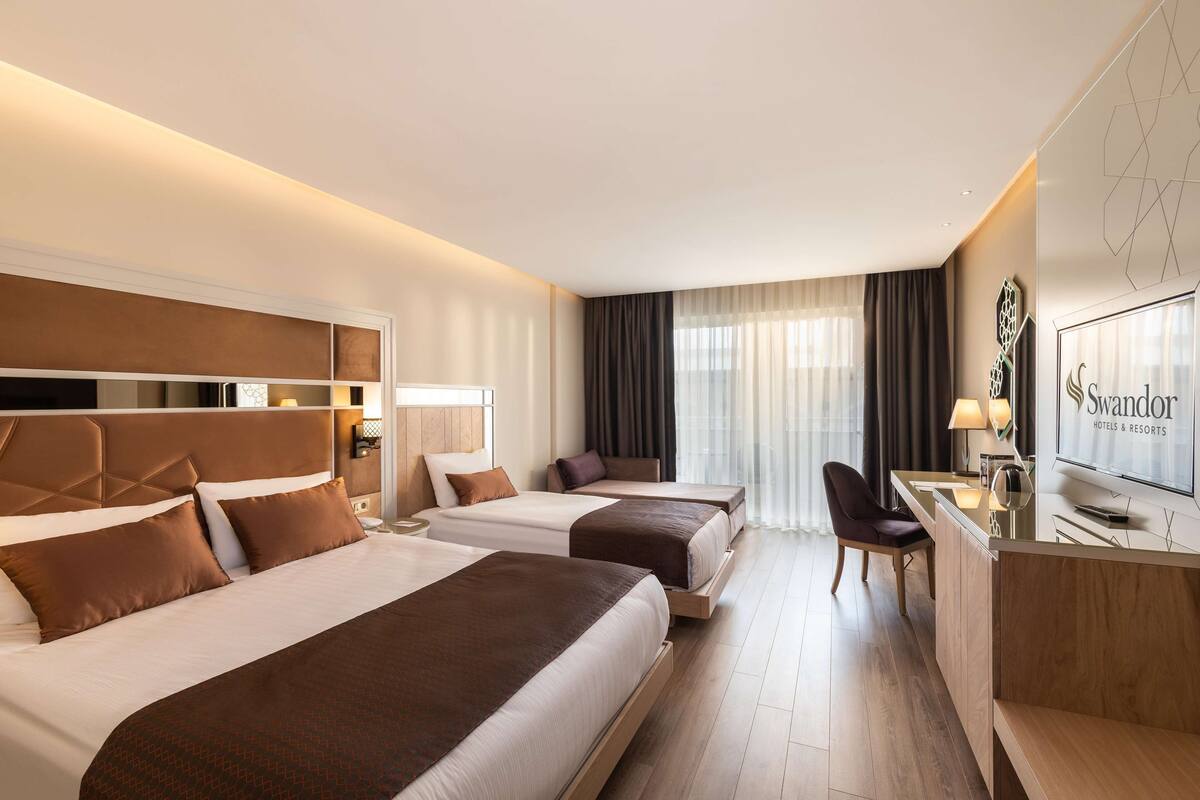Quarto de hotel com duas camas, uma escrivaninha, televisão e vista para a cidade.