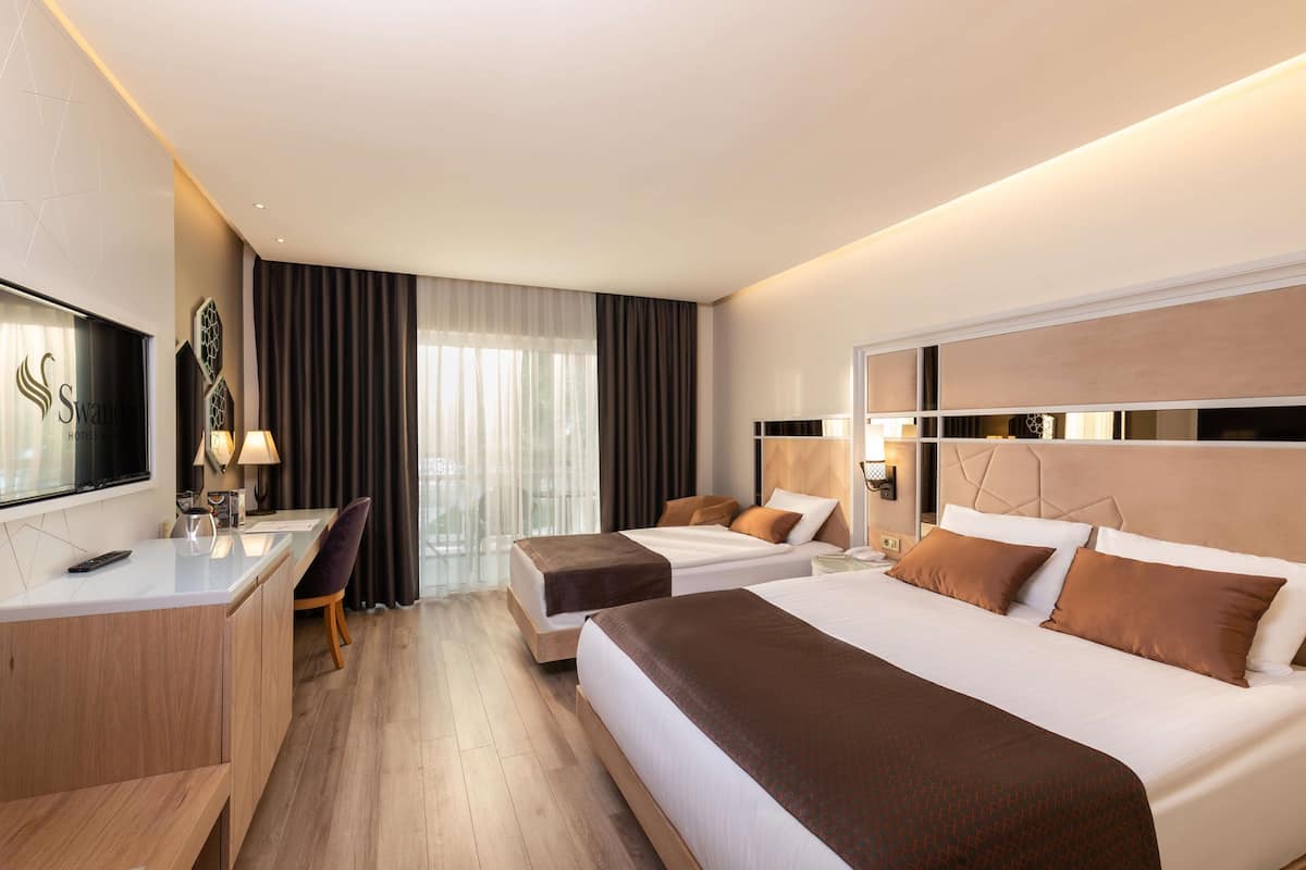 Quarto de hotel com duas camas, uma escrivaninha, uma televisão e uma janela com cortinas.