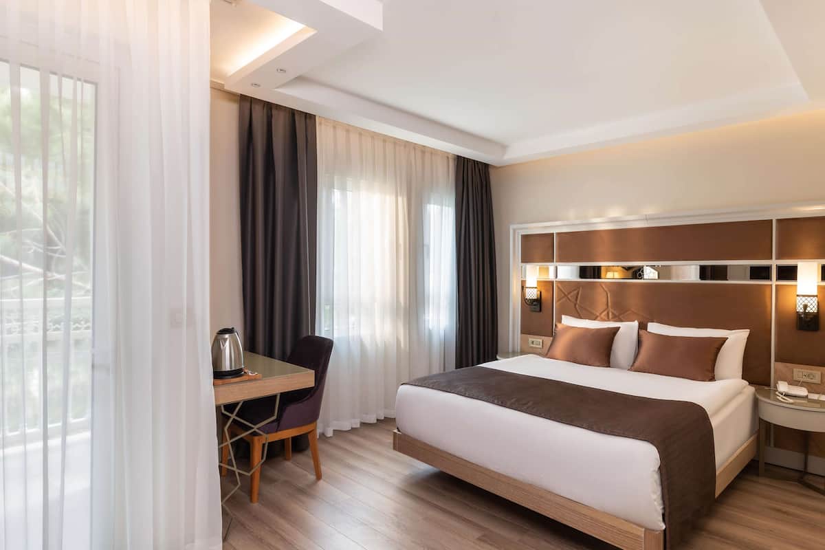 Quarto de hotel com uma cama grande, uma escrivaninha com cadeira, uma máquina de café e uma mesa de cabeceira com telefone.