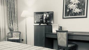 Quarto de hotel com uma cama, uma escrivaninha, uma cadeira, um abajur e um quadro na parede.