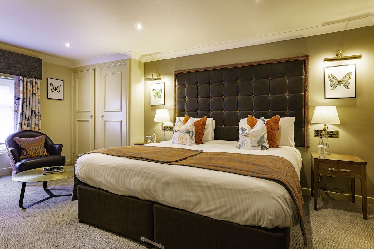 Quarto de hotel com uma cama grande, uma cadeira, uma mesa de cabeceira e uma luminária.