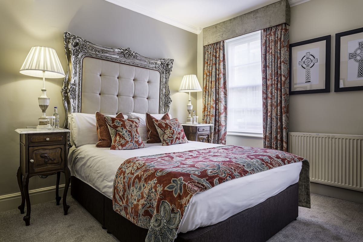 Quarto com cama grande, duas mesas de cabeceira, janela com cortinas e quadro na parede.