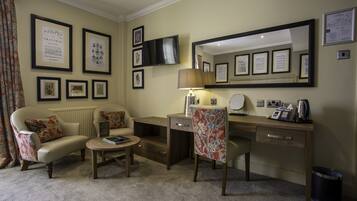 Quarto de hotel com sofá, poltrona, escrivaninha e um espelho grande.