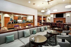 Um hall de hotel moderno com área de estar, bar e cozinha visíveis ao fundo.