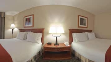 Quarto de hotel com duas camas, uma mesa de cabeceira com luminária e uma pequena mesa.