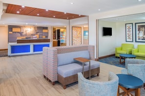 Um hall de hotel com área de estar, balcão de recepção e frigobar abastecido com bebidas.