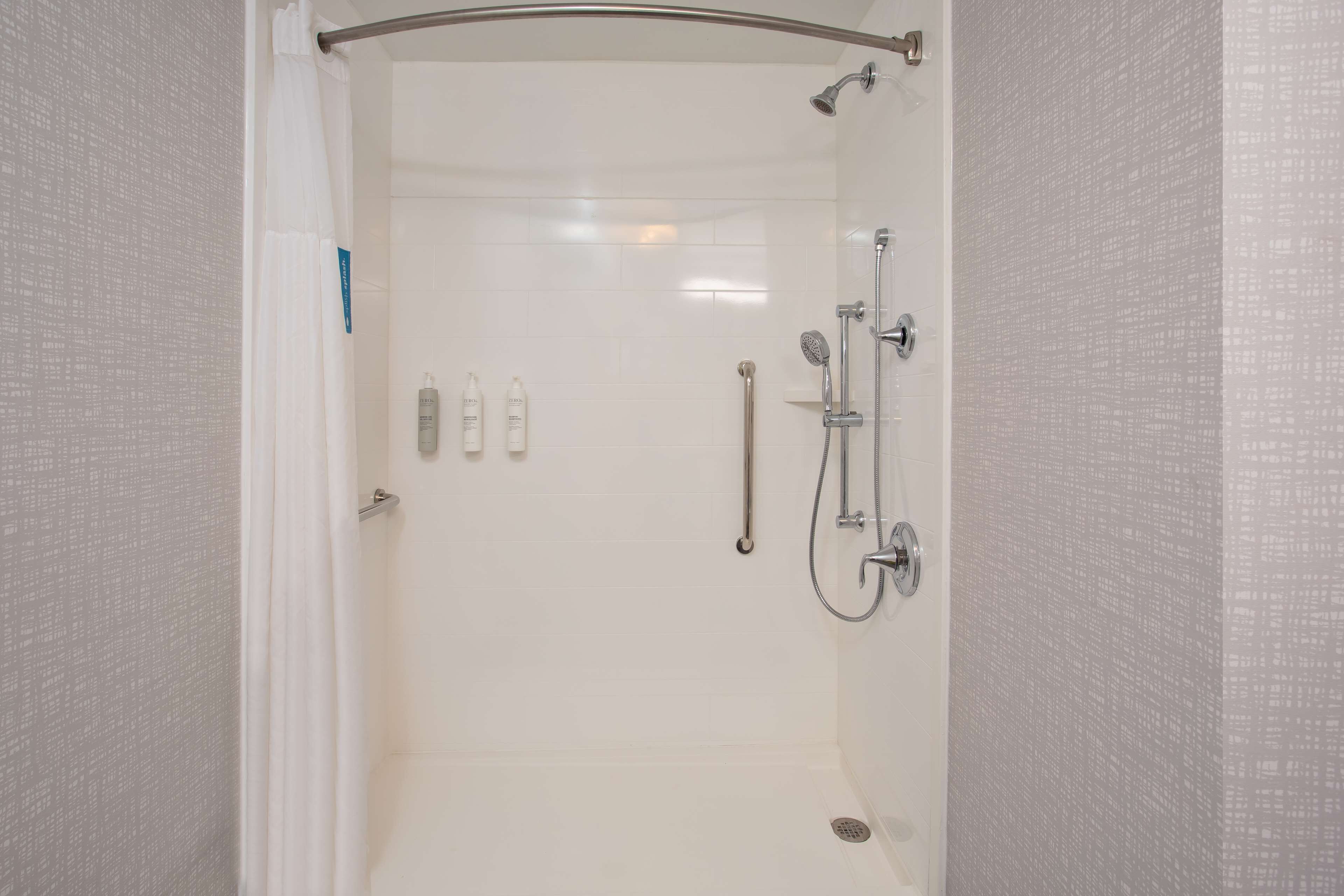 Um espaço de chuveiro moderno com porta de vidro, chuveiro manual, torneira na parede e dois frascos de shampoo.