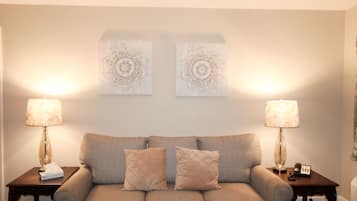 Uma sala de estar com um sofá bege, duas obras de arte decorativas e duas luminárias em mesas de apoio.