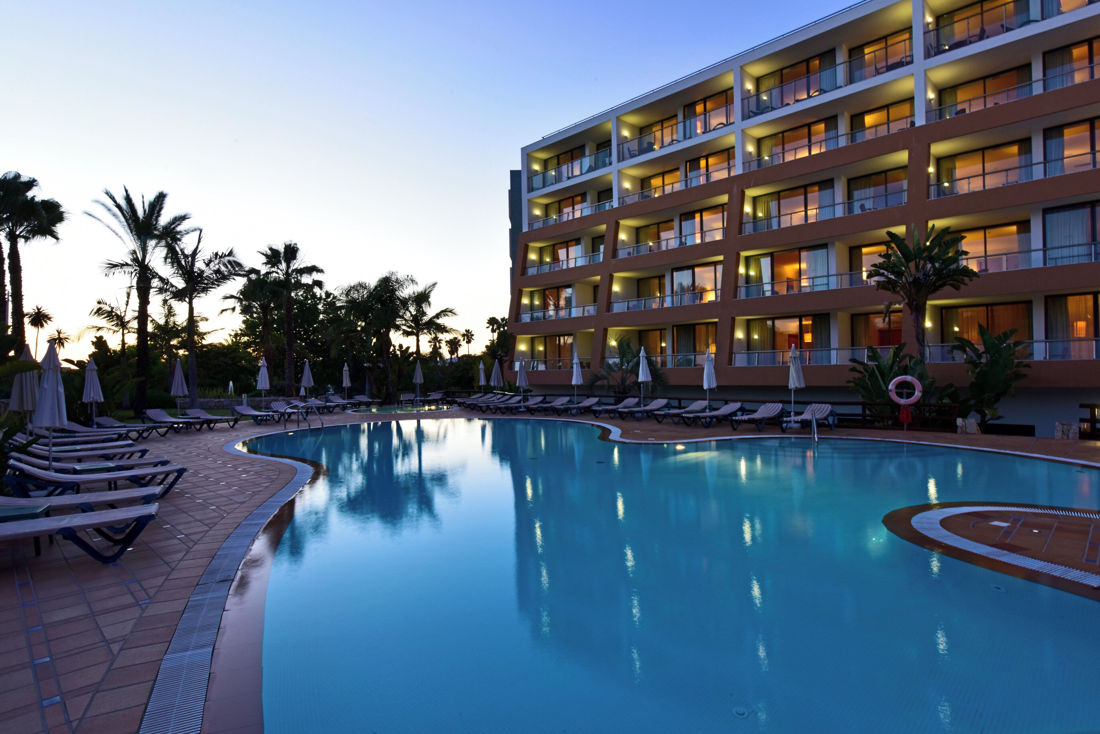 Um hotel com piscina, espreguiçadeiras e palmeiras.