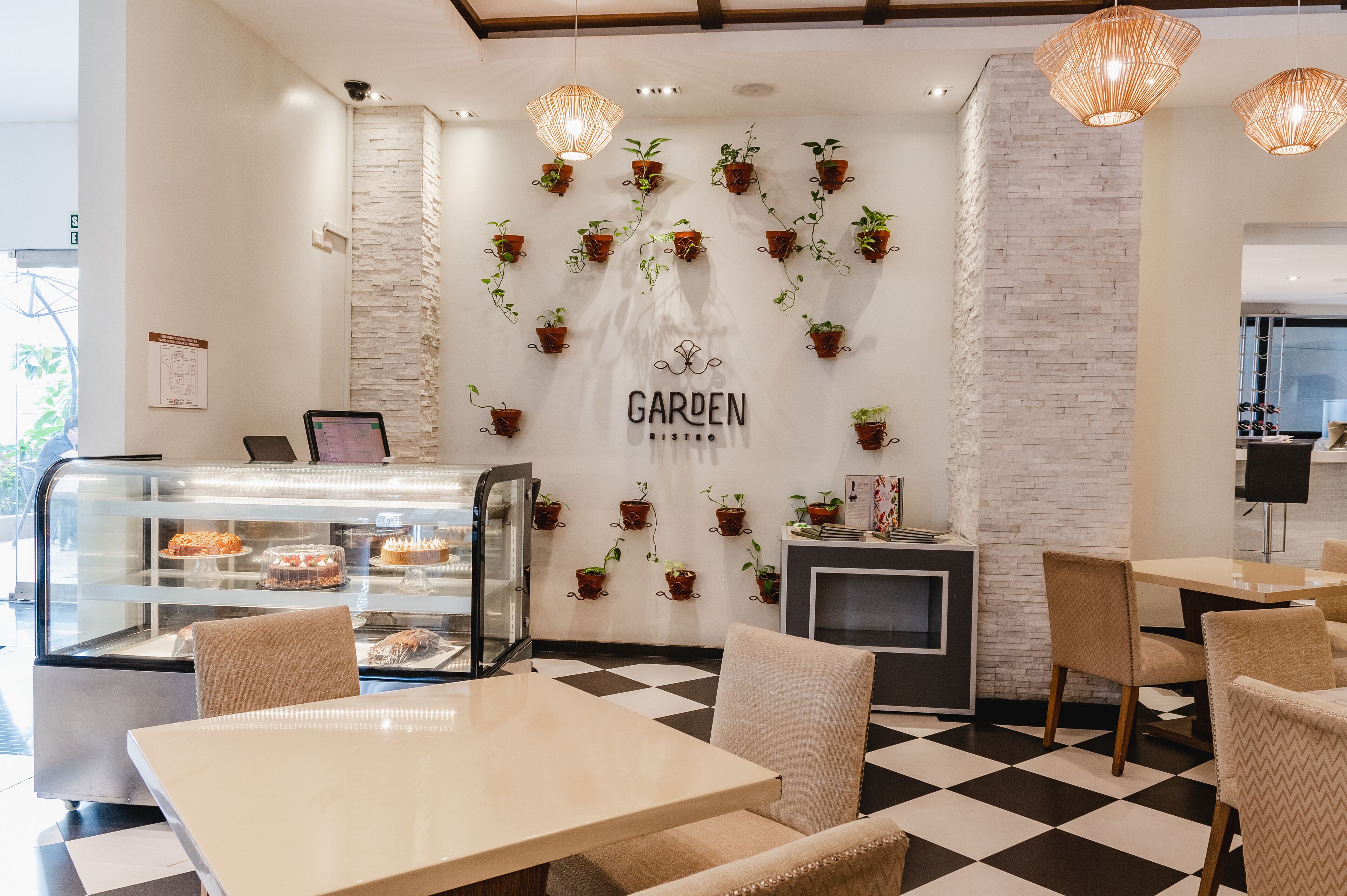 Um café com interior moderno, com chão quadriculado, cadeiras de madeira e plantas penduradas.