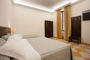 Quarto de hotel com duas camas, um guarda-roupa, um banco e uma TV fixada na parede.