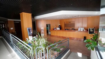 Uma área de recepção de hotel com balcão de mármore, um recepcionista e um balcão de atendimento.