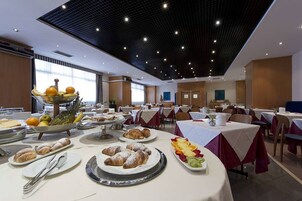 Uma sala de jantar ampla com várias mesas, uma exposição de frutas e uma variedade de doces.