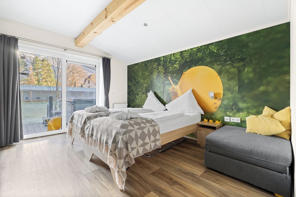 Um quarto com uma cama, um sofá, uma janela grande e um mural com uma cena de floresta.