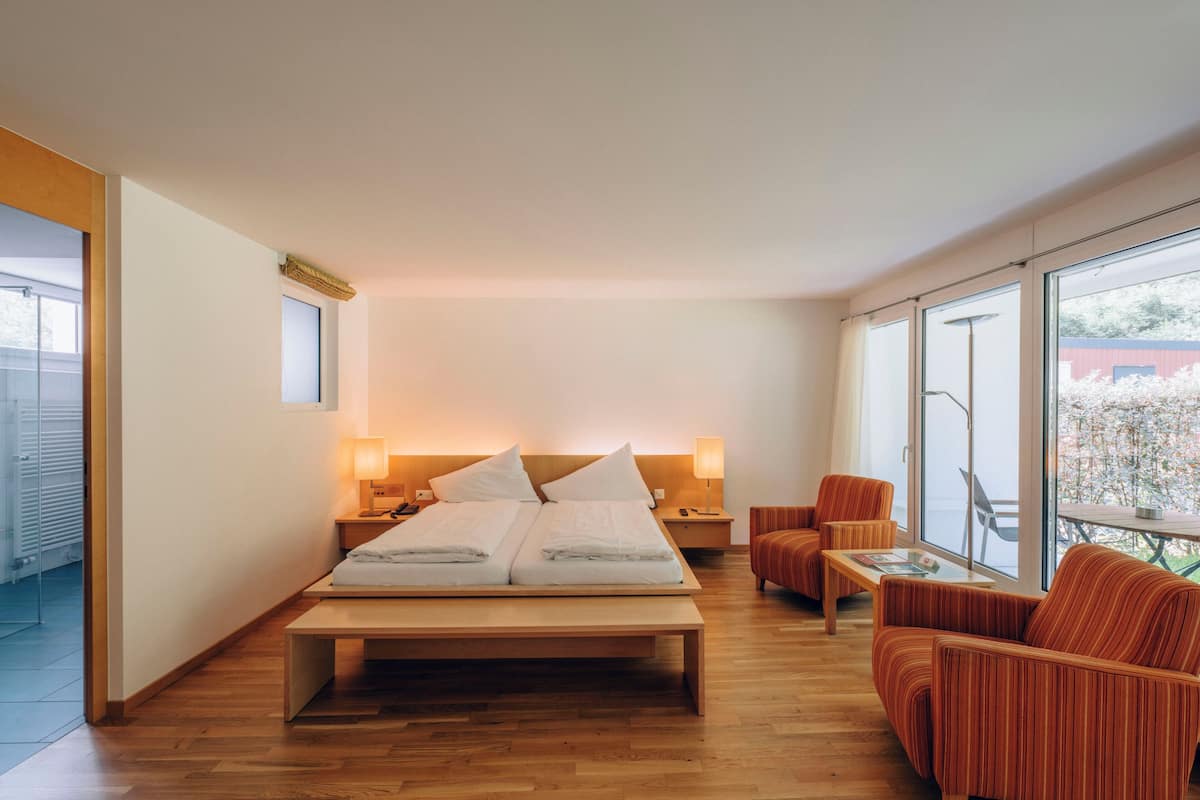 Quarto moderno com cama grande, mesas de cabeceira, um sofá e vista para o exterior.
