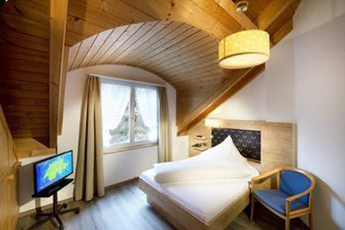 Quarto aconchegante com cama, poltrona, televisão e janela com cortinas.