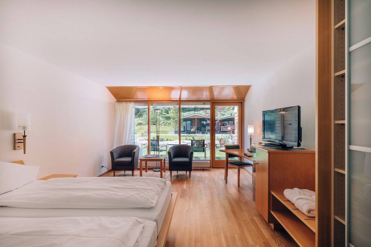 Quarto de hotel com cama, escrivaninha, cadeira, televisão e vista para o exterior.