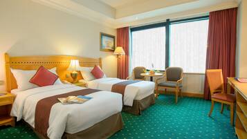 Quarto de hotel com duas camas, uma escrivaninha, uma cadeira, uma mesa e uma janela com cortinas.