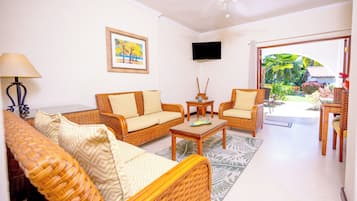 Uma sala de estar com móveis de vime, uma televisão de tela plana e vista para um jardim.