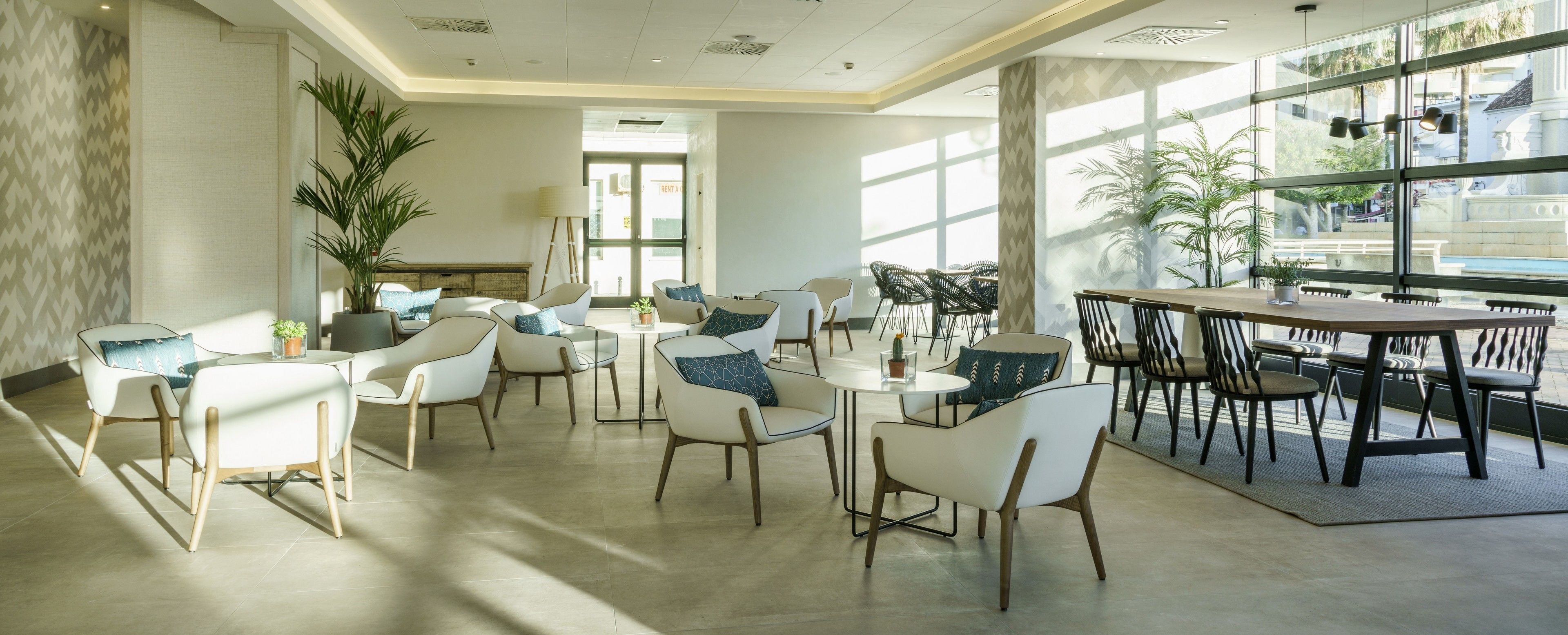 Uma sala de jantar moderna com cadeiras brancas e pretas, mesas redondas e grandes janelas que proporcionam luz natural.