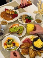 Uma mesa de café da manhã com diversos pratos, incluindo panquecas, frutas, croissants e ovos mexidos.