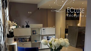 Uma área de recepção com design moderno, destacando uma cadeira azul, um balcão de recepção branco e um vaso com flores brancas.