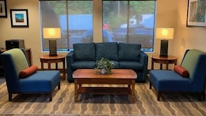 Um saguão de hotel com um conjunto de sofás, duas poltronas, uma mesa de centro e duas mesas laterais com luminárias.
