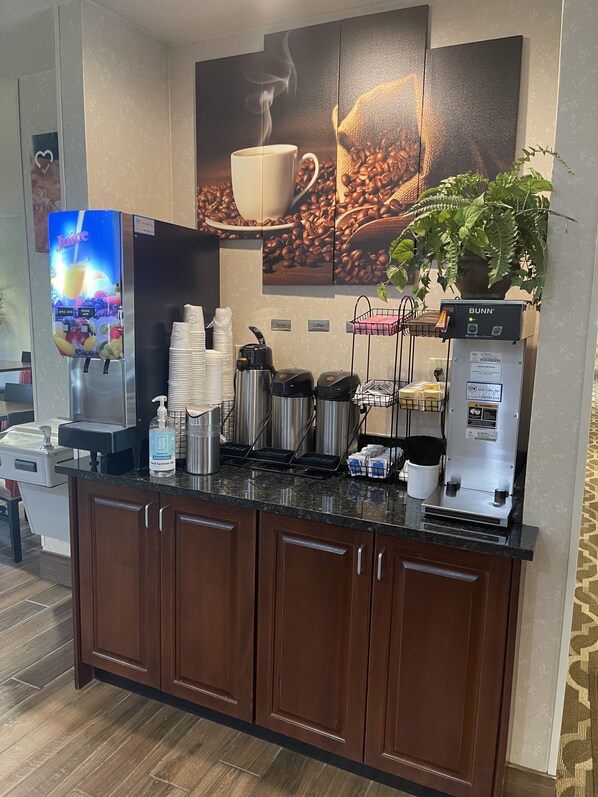 Uma área de recepção de hotel com uma máquina de café, um dispensador de suco e um dispensador de água.