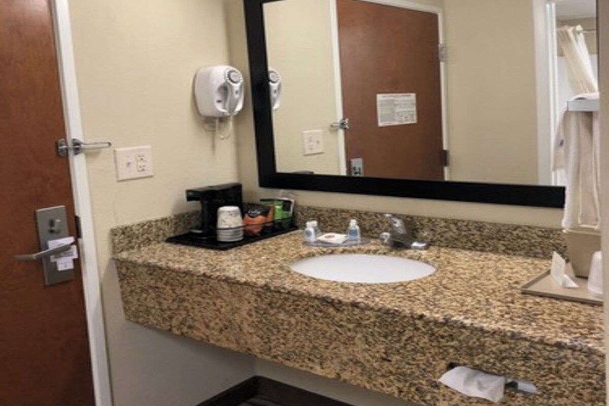 Casa de banho de hotel com bancada de granito, lavatório, espelho e porta-toalhas.