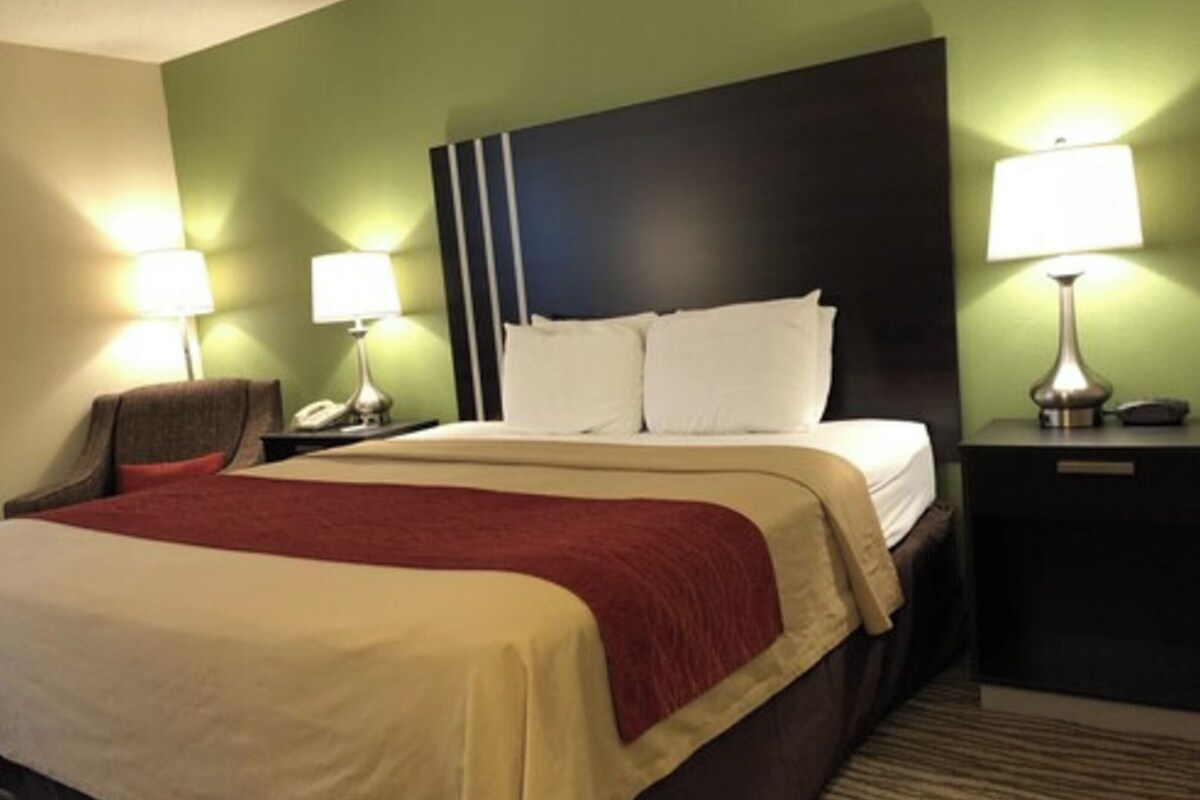 Quarto de hotel com cama, duas mesas de cabeceira, uma cadeira e uma luminária.