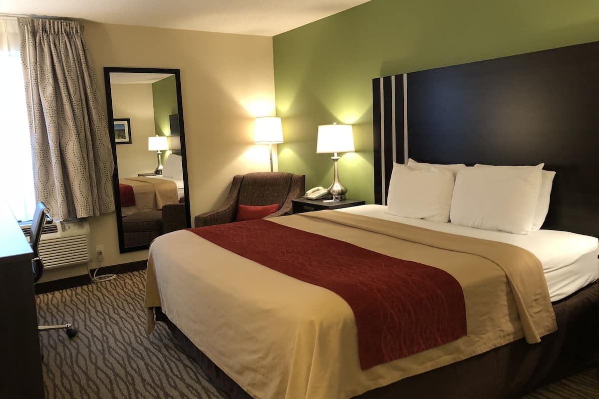 Quarto de hotel com uma cama grande, duas luminárias de cabeceira, uma cadeira, uma escrivaninha e um espelho.