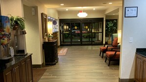 Um saguão de hotel com piso de madeira, balcão de recepção, área de estar e entrada por porta de vidro.