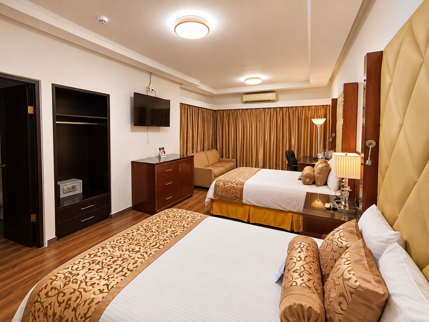 Quarto de hotel com duas camas, uma televisão, uma escrivaninha com luminária e um guarda-roupa.