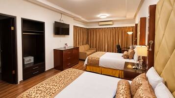 Quarto de hotel com duas camas, uma televisão, uma escrivaninha com luminária e um guarda-roupa.