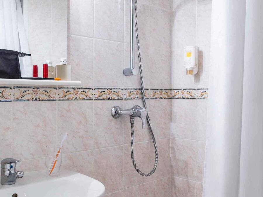 Casa de banho com chuveiro, lavatório e produtos de higiene num armário.
