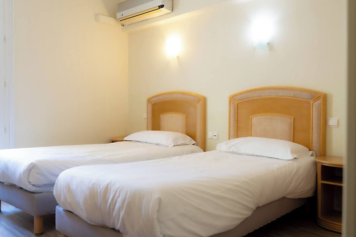 Duas camas de solteiro com cabeceiras de madeira e roupa de cama branca num quarto de hotel.