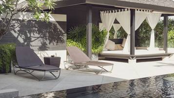 Área da piscina com duas espreguiçadeiras e um espaço coberto para sentar com vista para a piscina.