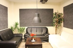 Uma sala de estar moderna com um sofá de couro preto, um sofá branco, uma mesa de centro de madeira com um vaso de flores e uma luminária pendente.
