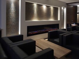 Uma área de estar moderna com assentos de couro preto, uma mesa de madeira e uma TV na parede exibindo uma vista urbana.