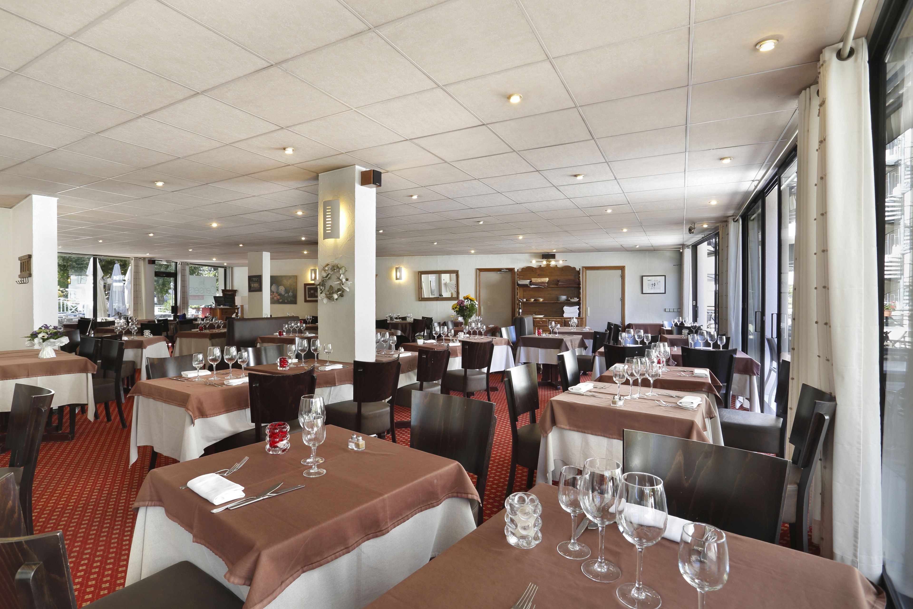 Um restaurante espaçoso com várias mesas e cadeiras, janelas amplas e teto alto.